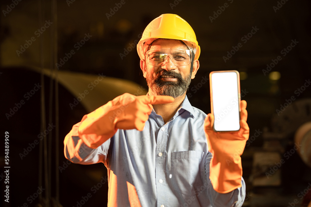 Indian male engineer wearing yellow helmet showing smart phone with ...