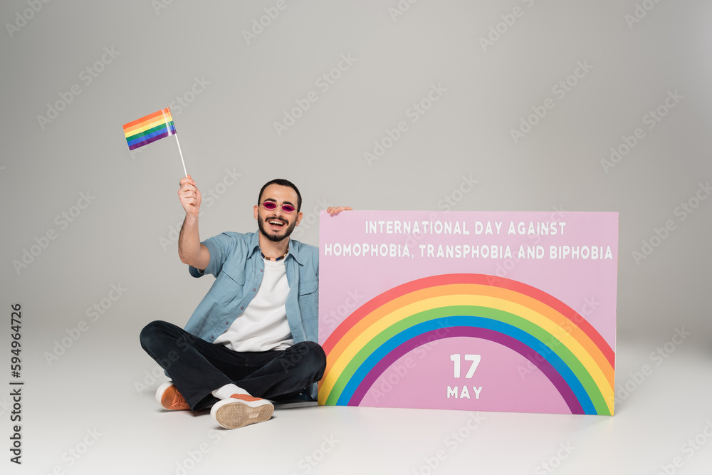 Positive gay man holding lgbt flag near placard with International Day ...