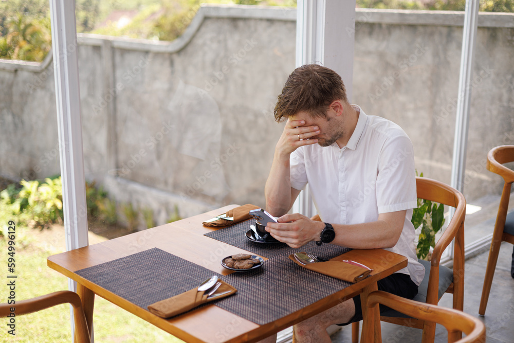 A tired man in a white shirt is sitting in a cafe. Summer heat ...