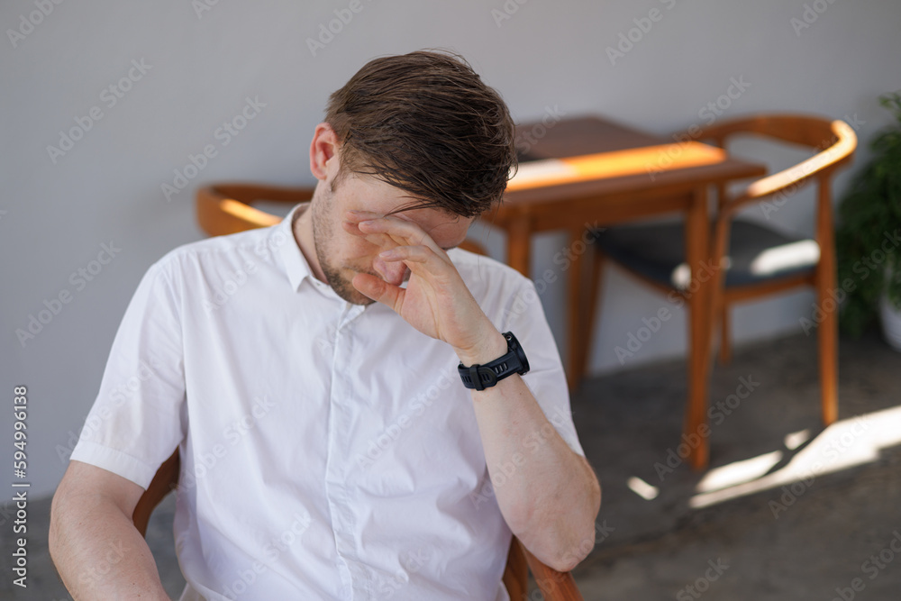 A tired man in a white shirt is sitting in a cafe. Summer heat ...