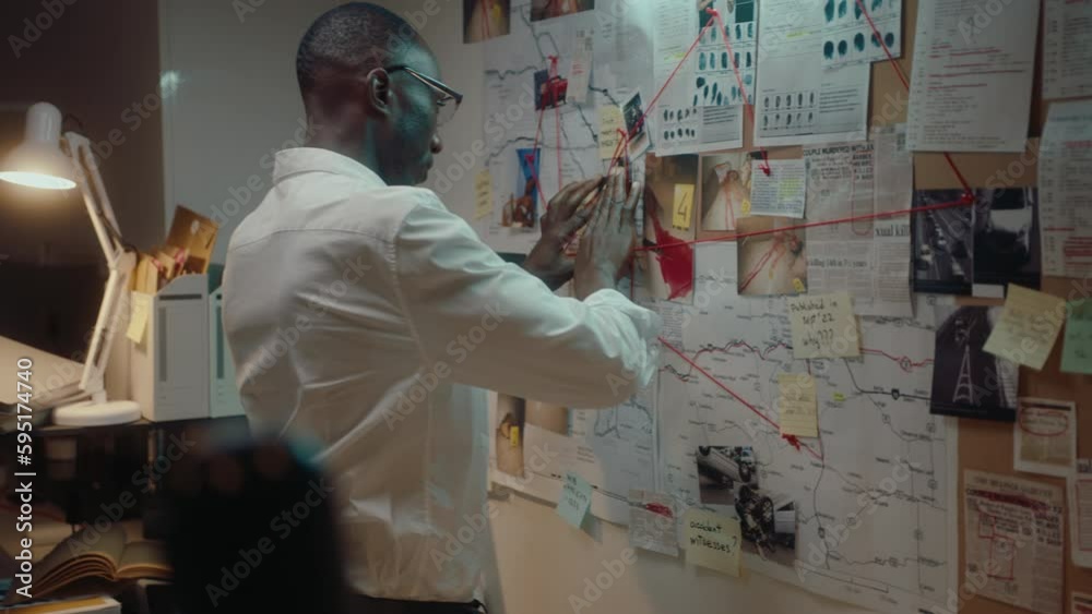African American male detective pinning crime scene photo to board on ...