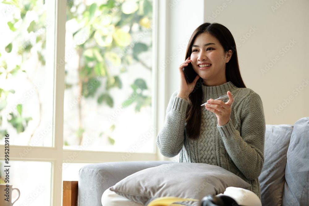 Young chinese girl talking on the smartphone sitting on the sofa at ...