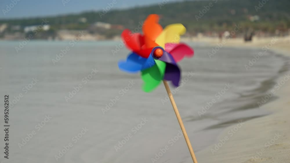 Vibrant pinwheel rotates under the blowing wind on a sandy sea beach ...