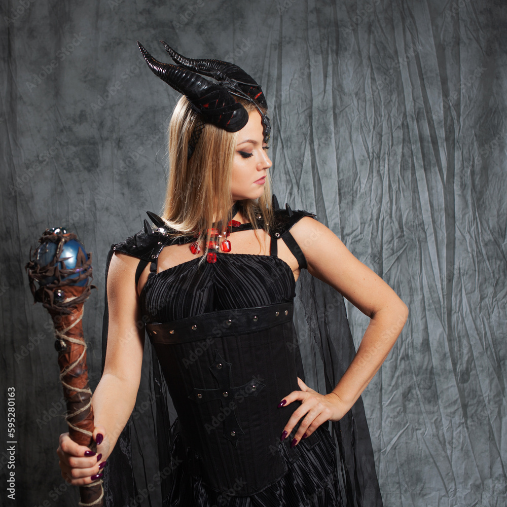magical lady in a long black dress and with demon horns, studio gray ...