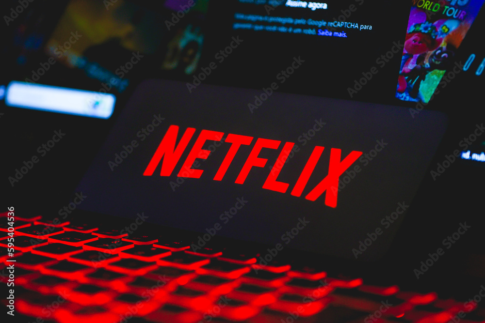 The Netflix logo on a cell phone screen resting on top of a lighted ...