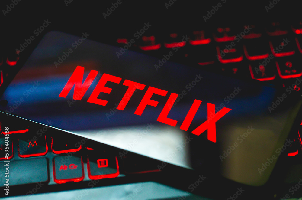 The Netflix logo on a cell phone screen resting on top of a lighted ...