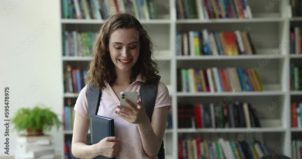 Pretty girl student use smartphone, search useful information on internet standing in library ...
