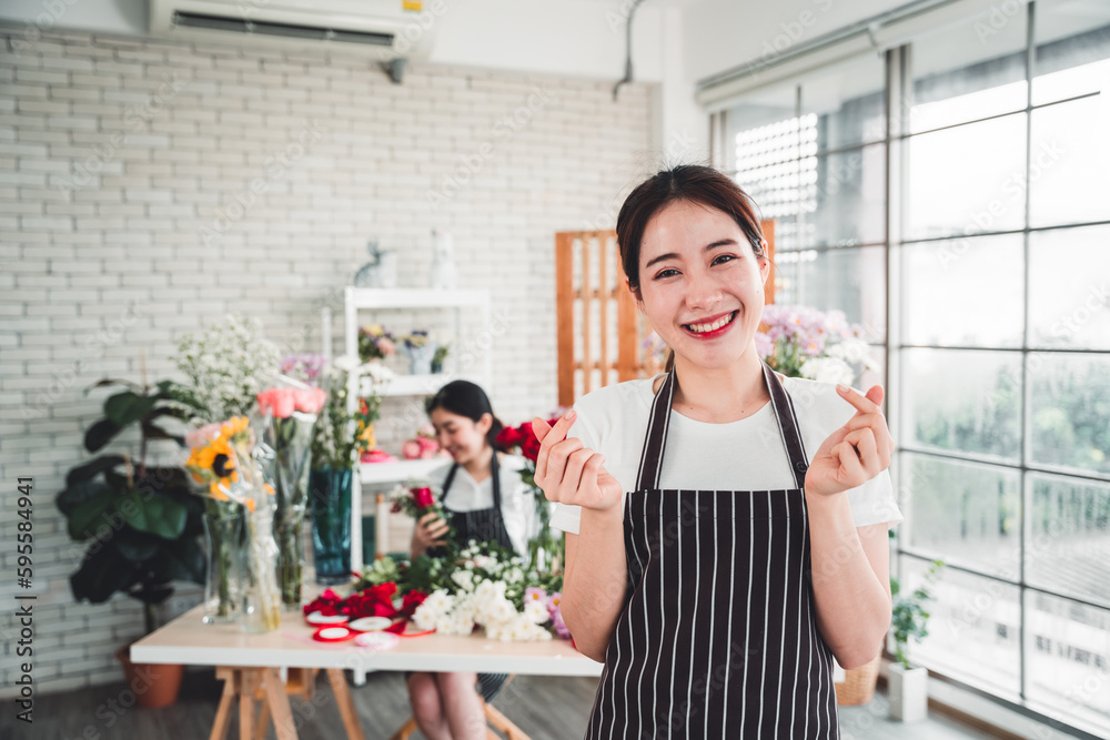Female florists sit in a flower shop and make miniheart hand gestures ...