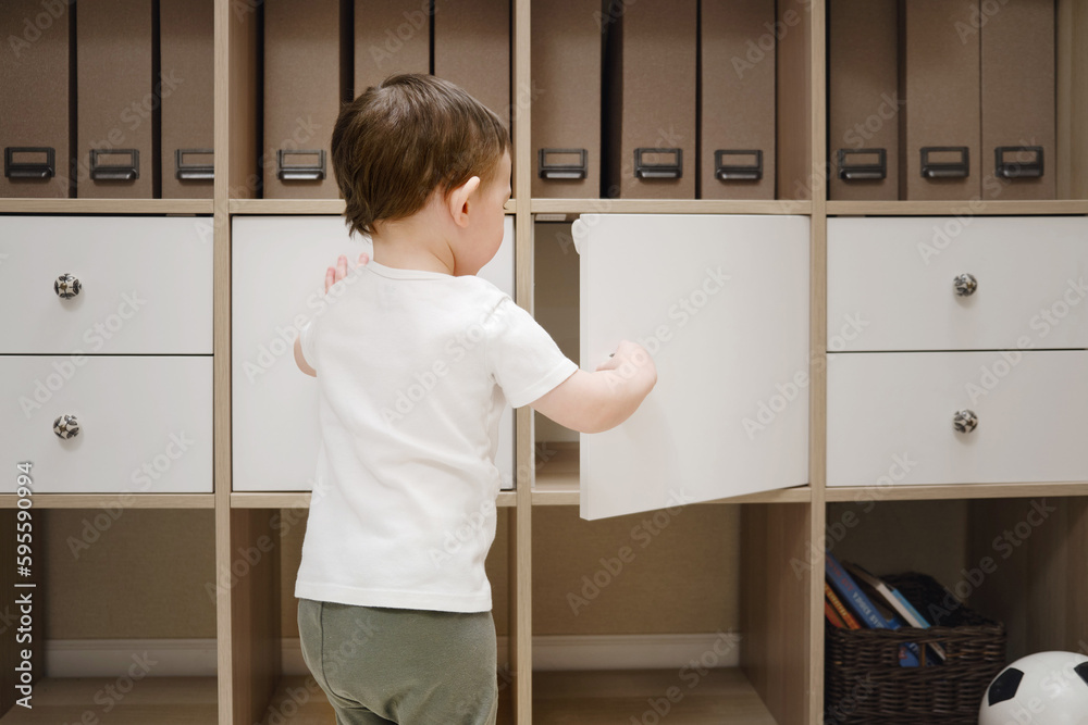 Toddler baby opens the closet door in the home living room. A small ...