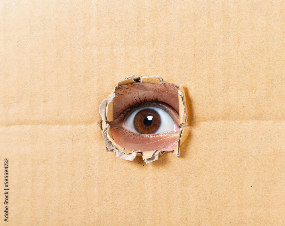 Foto de Hidden eye spying through torn hole in cardboard paper. Detective or spying concept ...