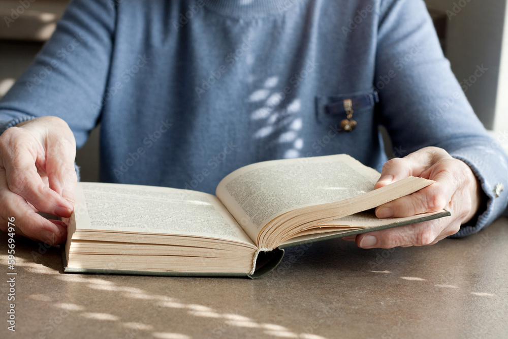 Closeup of elderly woman hand sitting at table reading an fiction book ...