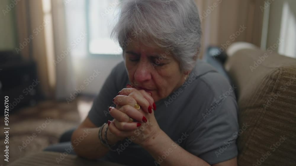Elderly woman praying to God at home sitting on couch. Dramatic scene ...