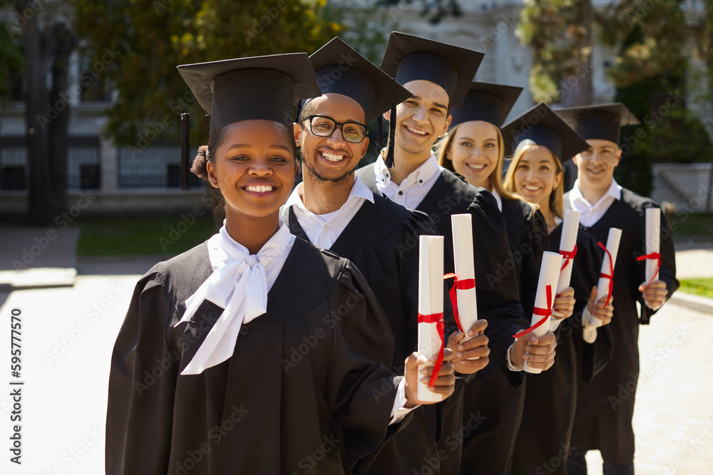 Laughing excited group of multicultural people in graduation gowns caps ...