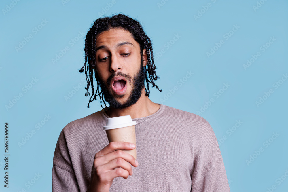 Surprised arab man holding coffee to go and looking at paper mug lid ...