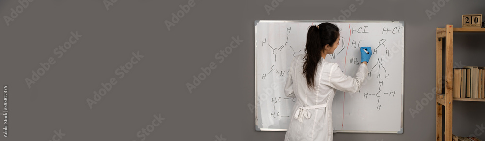 Rear view of chemistry teacher who draws on the blackboard formulas and ...