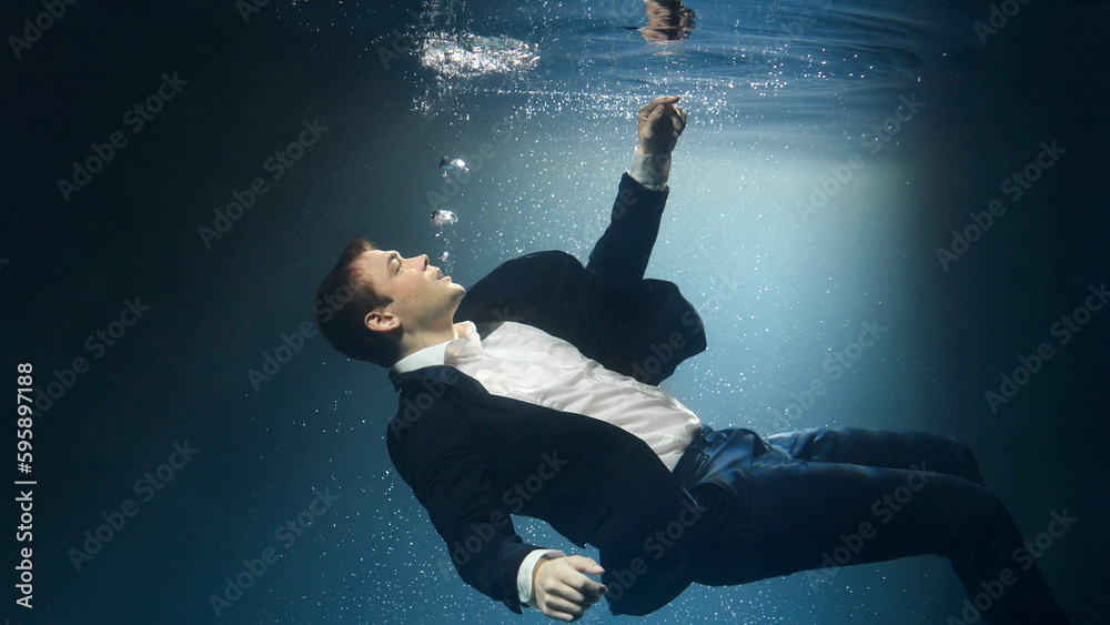Businessman, a man in a suit, is drowning under water, reaching for the ...