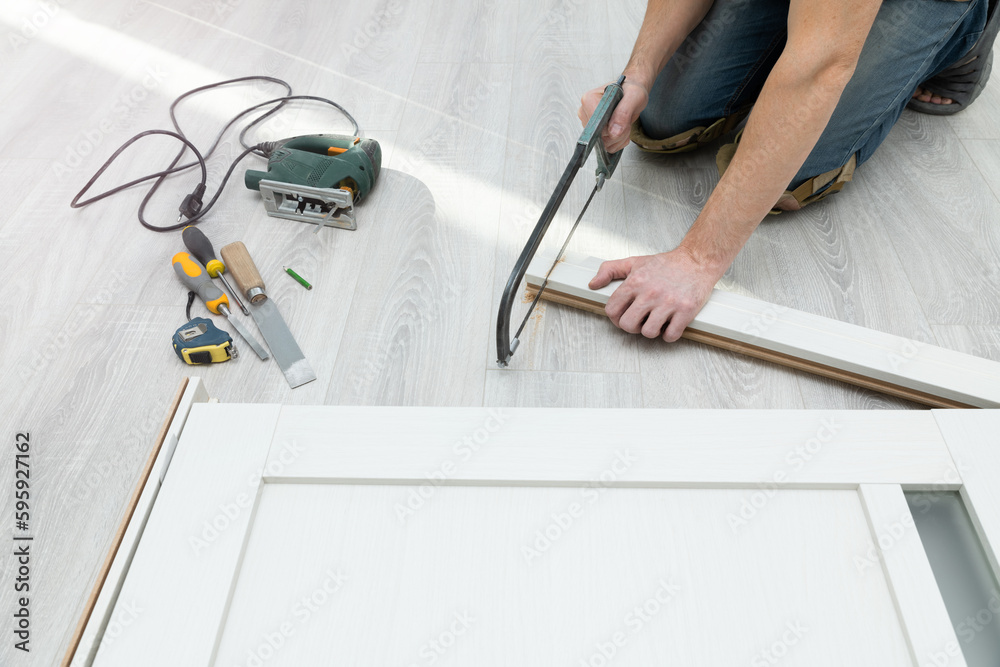 Worker assembles a door frame by cutting off the part with a hand saw ...