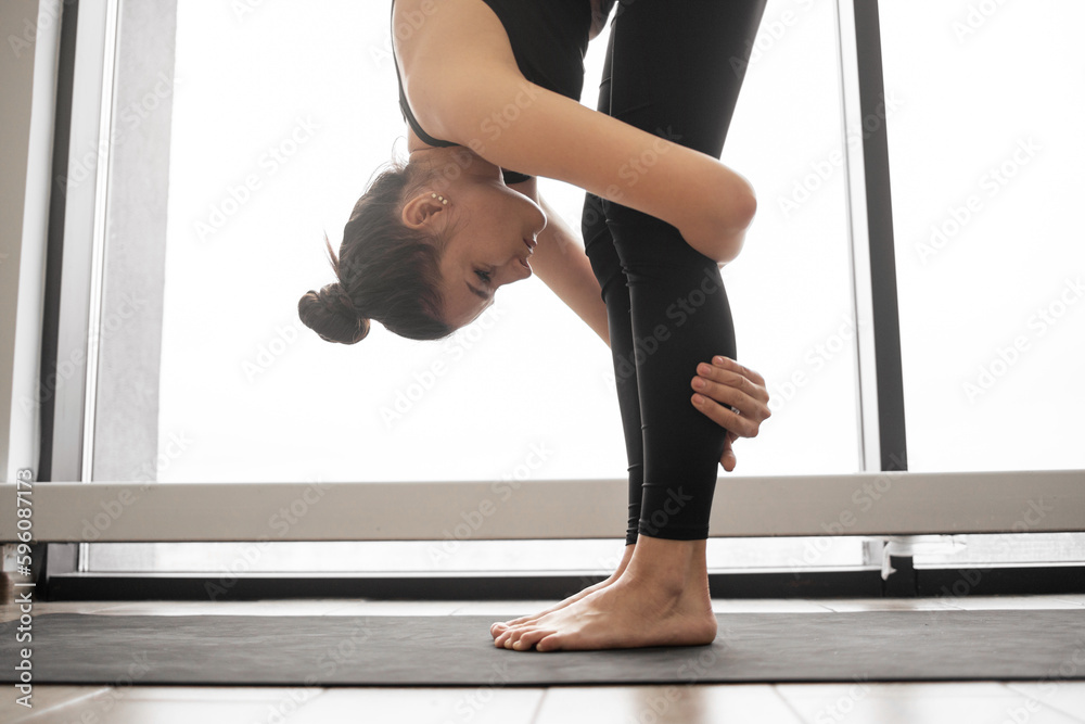 Crop view of slim young woman in black sportswear embracing legs and ...