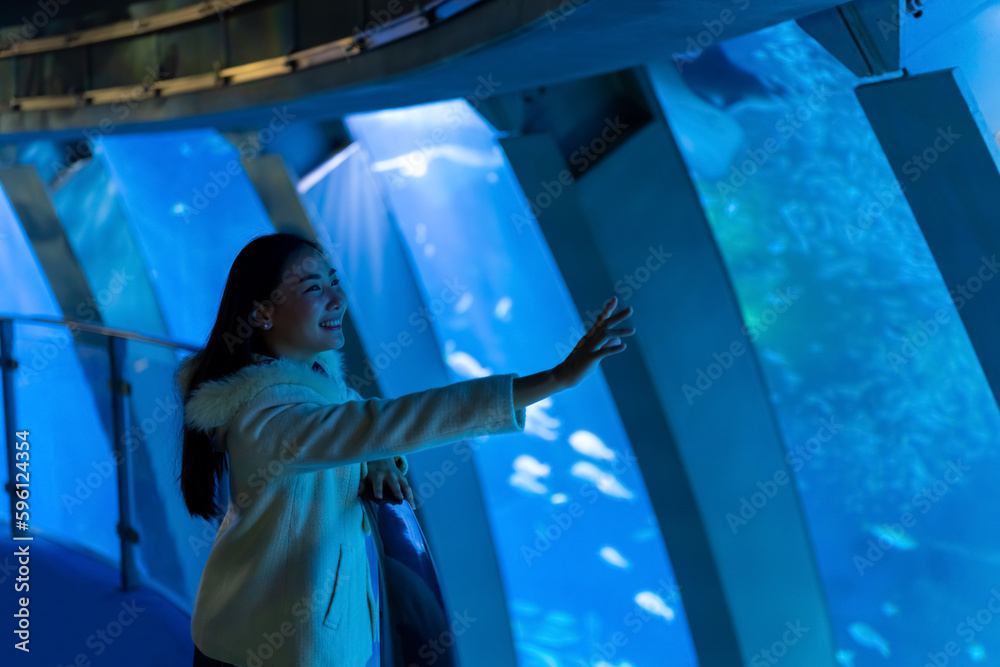 Young Asian woman looking shoal of fish in large glass tank during ...