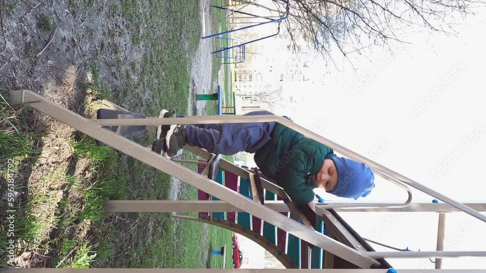 Vertical video - a cautious child descends the stairs on the playground ...