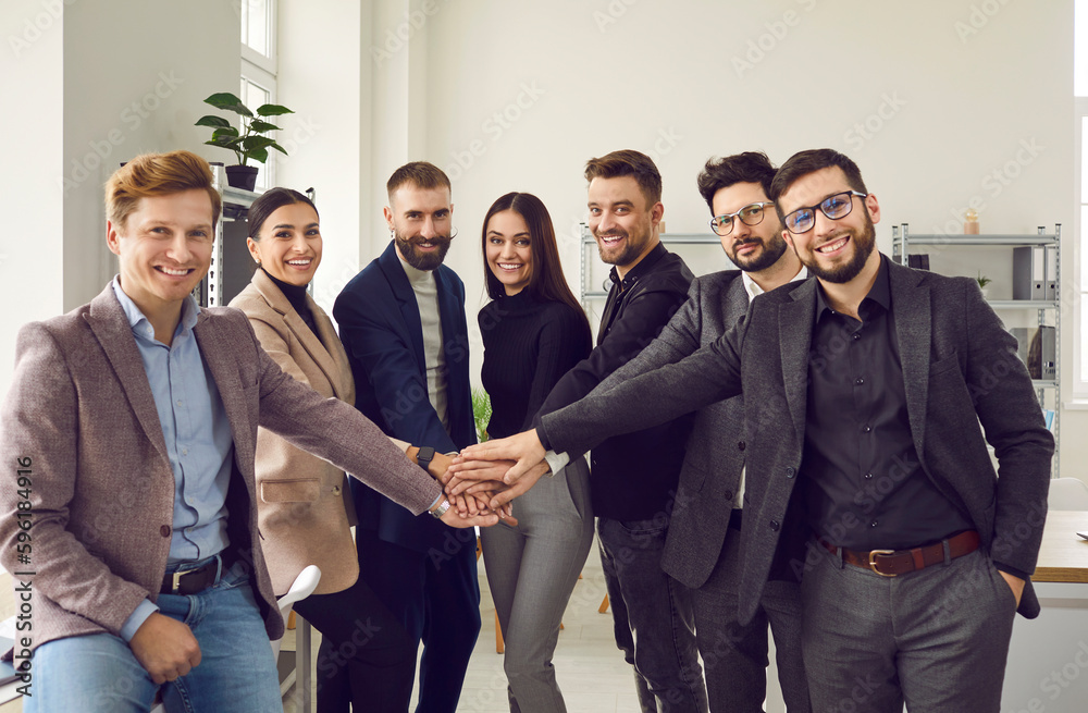 Smiling coworkers putting their hands together in office. Portrait of ...