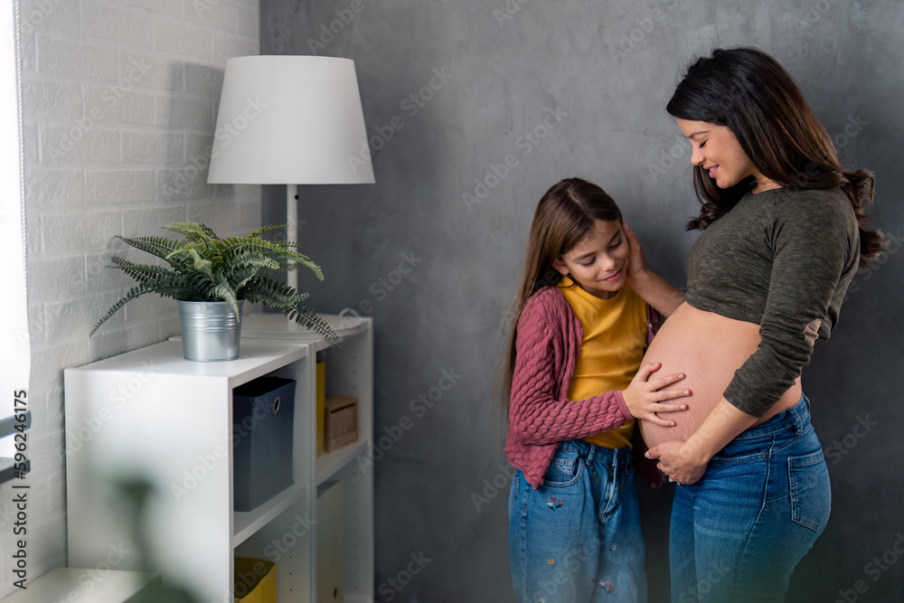 Young female child holding hands on mother's pregnant stomach awaiting ...