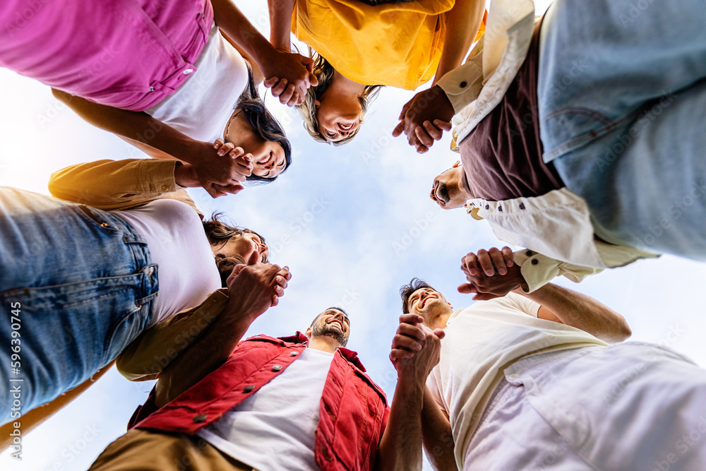 Low angle view of united group of young people in circle holding hands ...