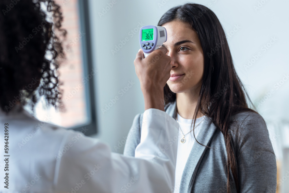 Cheerful beautiful female doctor taking woman patient temperature with ...