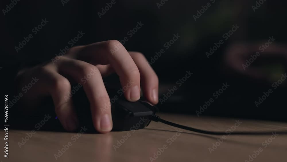 Close up of man gamer hands using computer mouse is playing video game at night. Male hacker ...