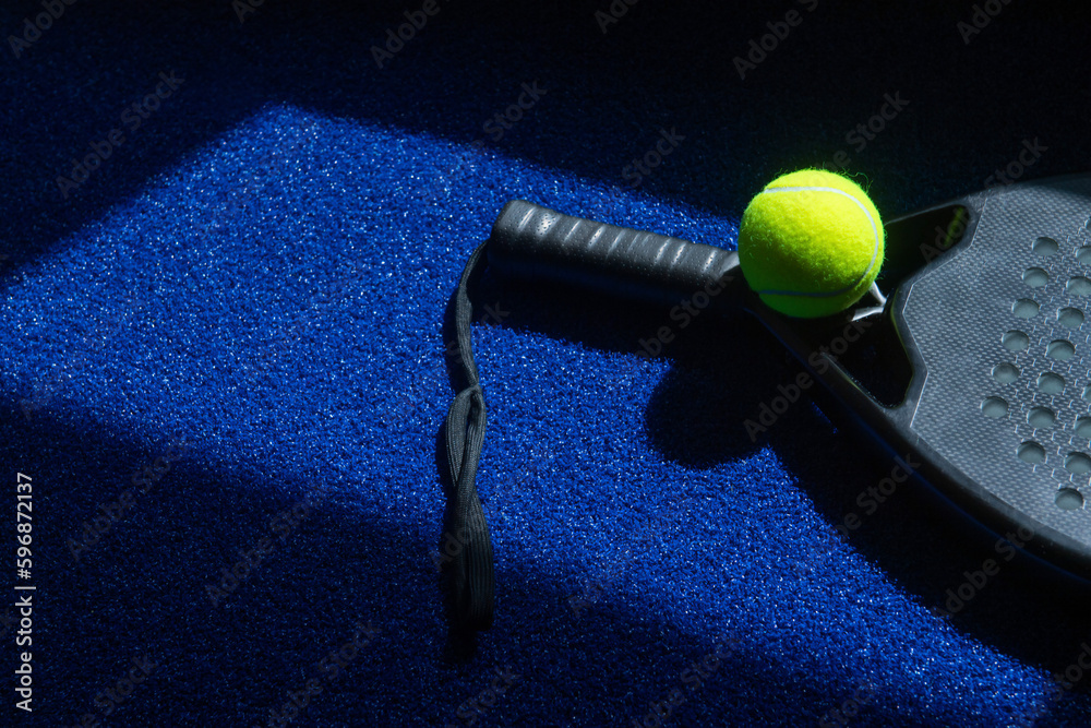 Black professional paddle tennis racket and ball with natural lighting ...