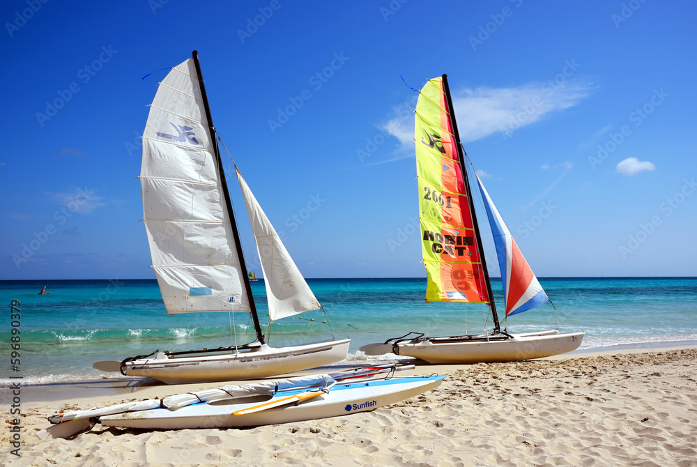 Two sail boats, catamaran, with one canoe on tropical beach with blue ...