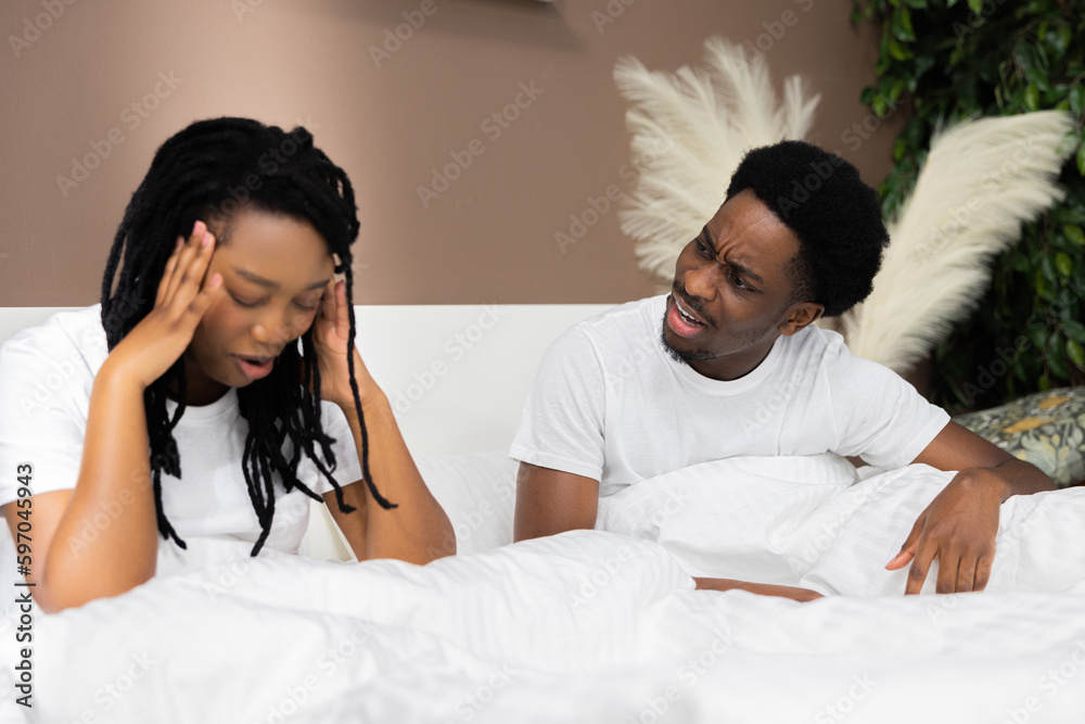 Dissatisfied angry unhappy African American dark skinned black couple sitting in bed in the ...