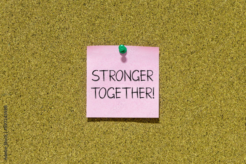 Stronger together text on pink post-it paper pinned on bulletin cork ...