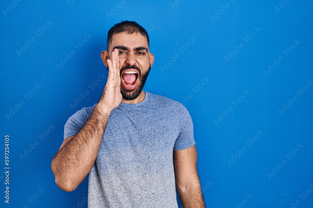 Middle east man with beard standing over blue background shouting and ...