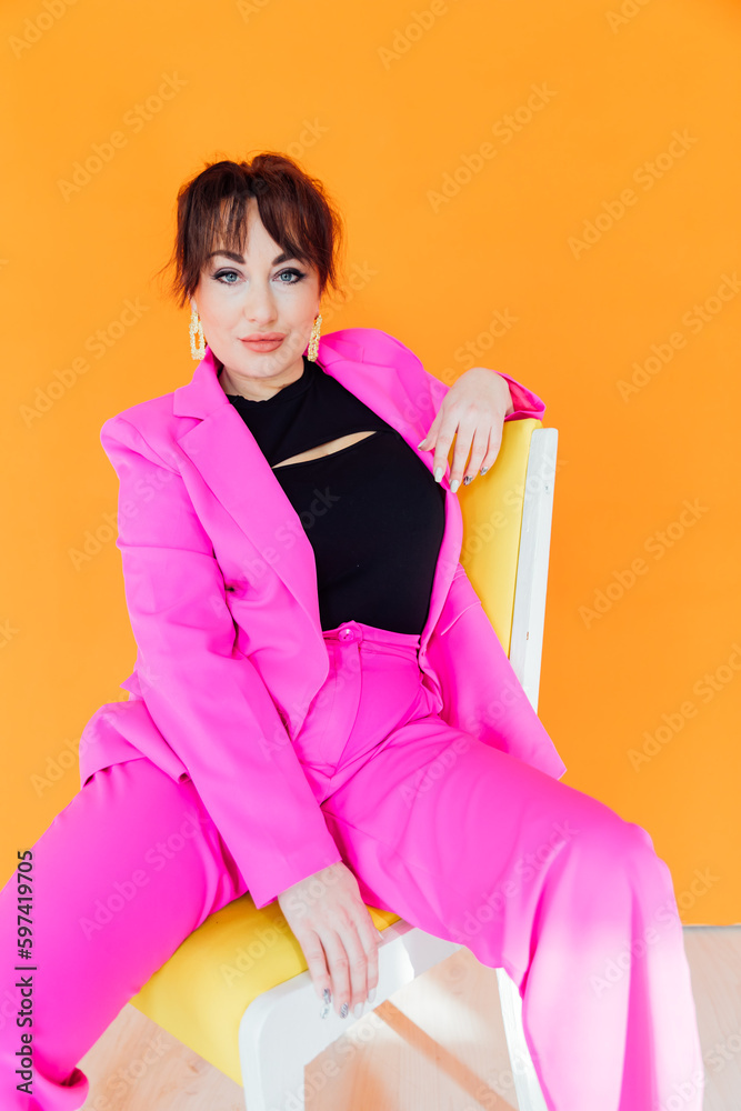 beautiful woman in bright clothes on a chair on an orange background ...