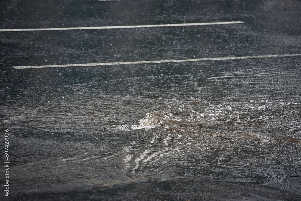 Flooded asphalt road with large puddle during heavy rain. Water drains ...