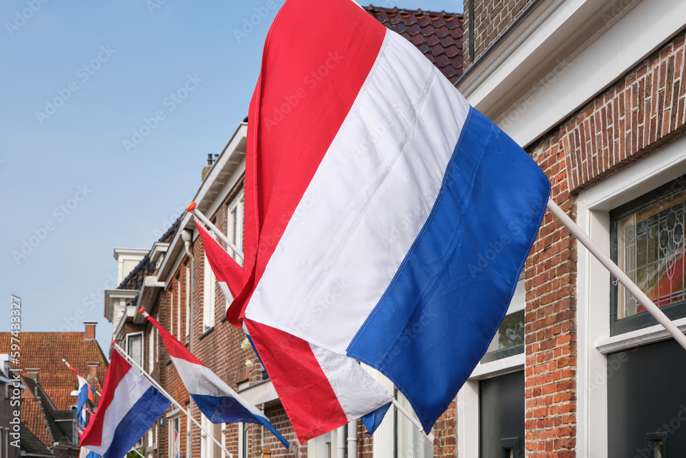 Dutch flags waving in a typical dutch street on Koningsdag under a blue ...