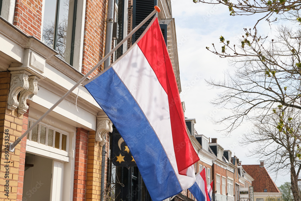 Dutch flags waving in a typical dutch street on Koningsdag under a blue ...