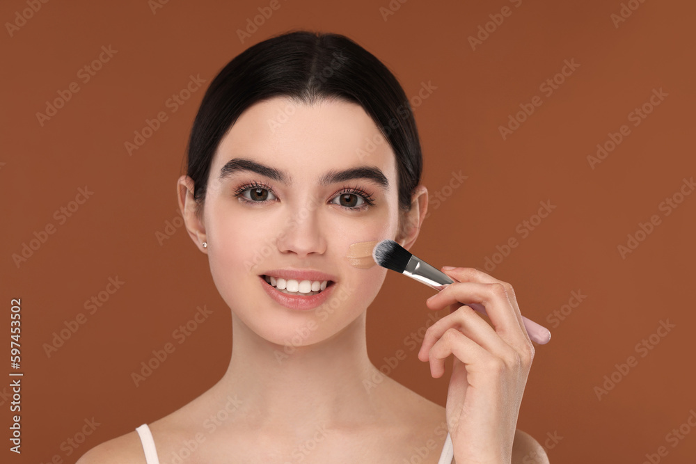 Teenage girl applying foundation on face with brush against brown ...