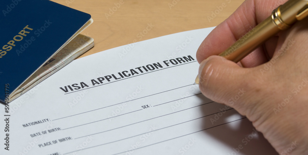 hand holding a pen writing a visa application form. Form and passport ...