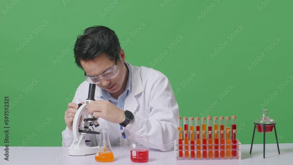 Asian Man Scientist Looking Through A Microscope On The Table With Test ...