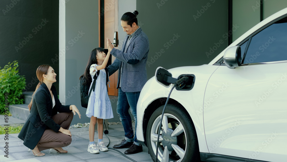 Progressive young parents and daughter with electric vehicle and home ...