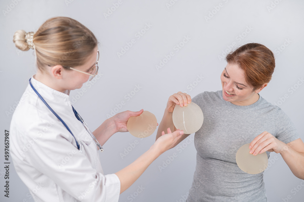 Caucasian woman trying on breast implants. A plastic surgeon helps a ...