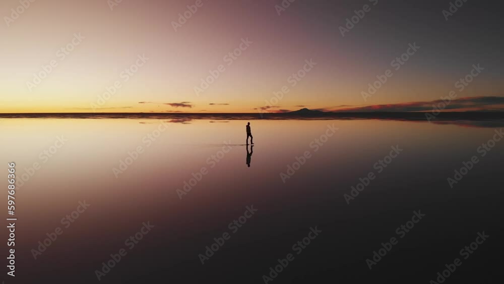 Aerial of a lone figure walking along the mirrored reflection of the ...