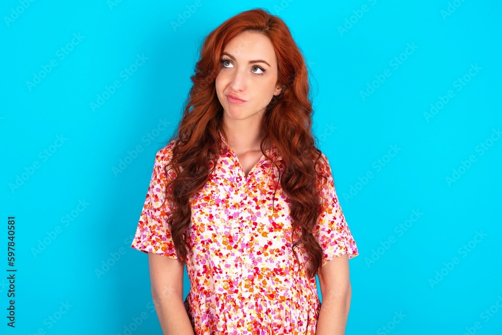 Caucasian redhead woman wearing floral dress over blue background has ...