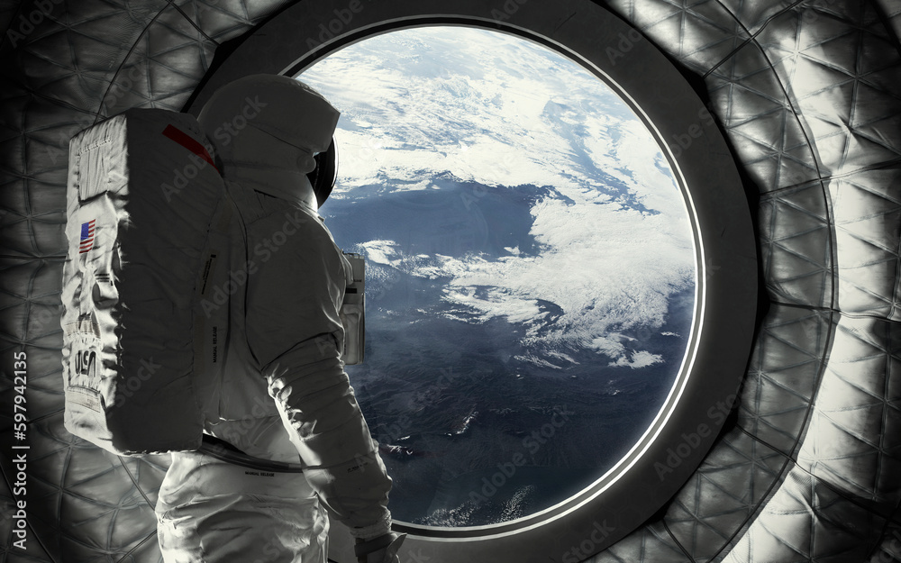 An astronaut stands at the huge window of a spaceship and looks at ...