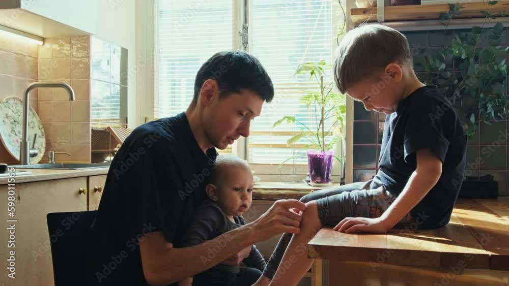 The child has hit his knee and needs help. The father seals the wound ...