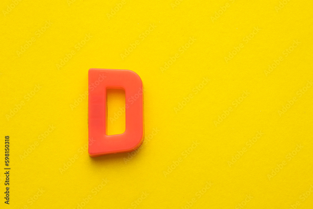 Peach colored plastic letter D uppercase on yellow foamy background ...