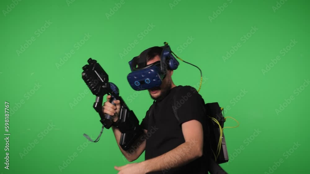 A man is playing a virtual game with a fake weapon on a green ...