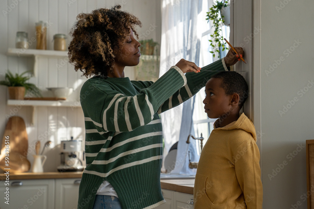 Caring african american mother measures changes height of child son on ...